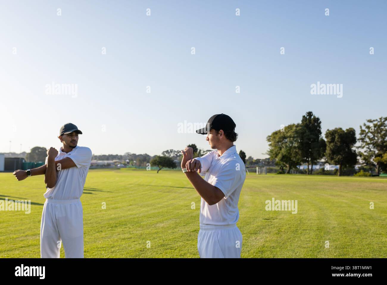 Diverse male teammates stretching across chest on cricket field in ...
