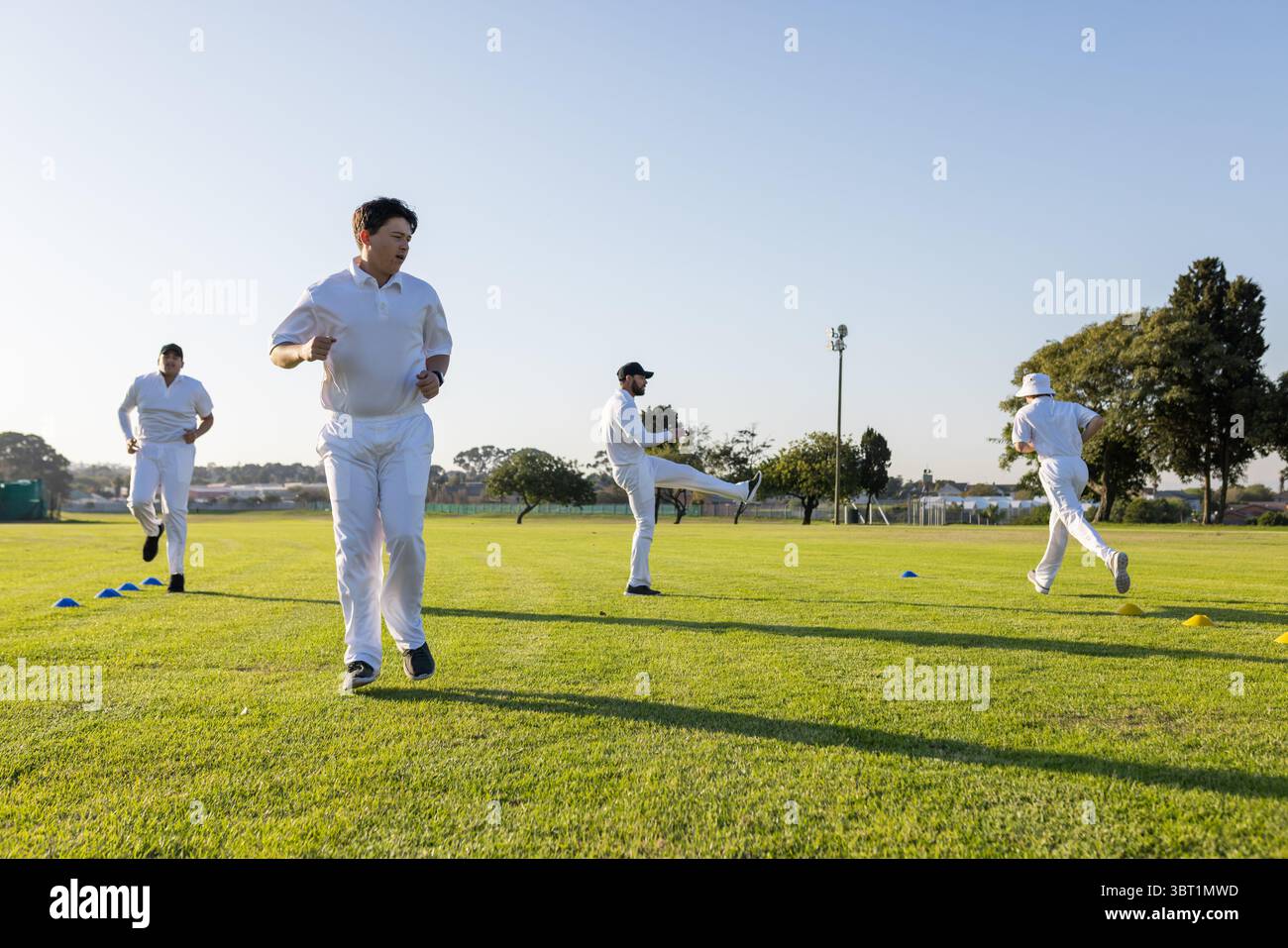 Male teammates in white uniforms running through cone lanes on sports ...