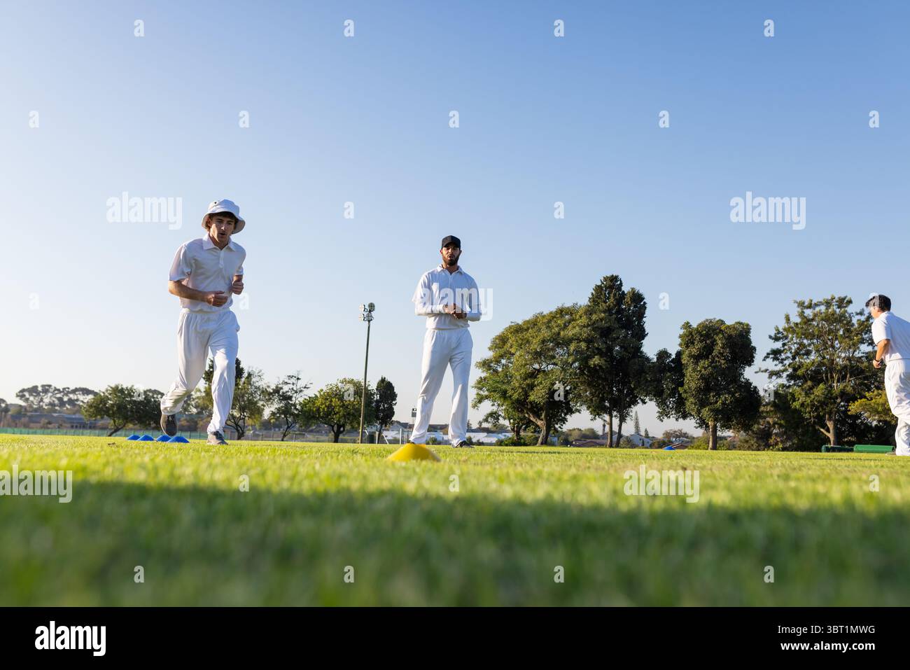 Diverse male teammates practicing fielding drills on cricket ground ...