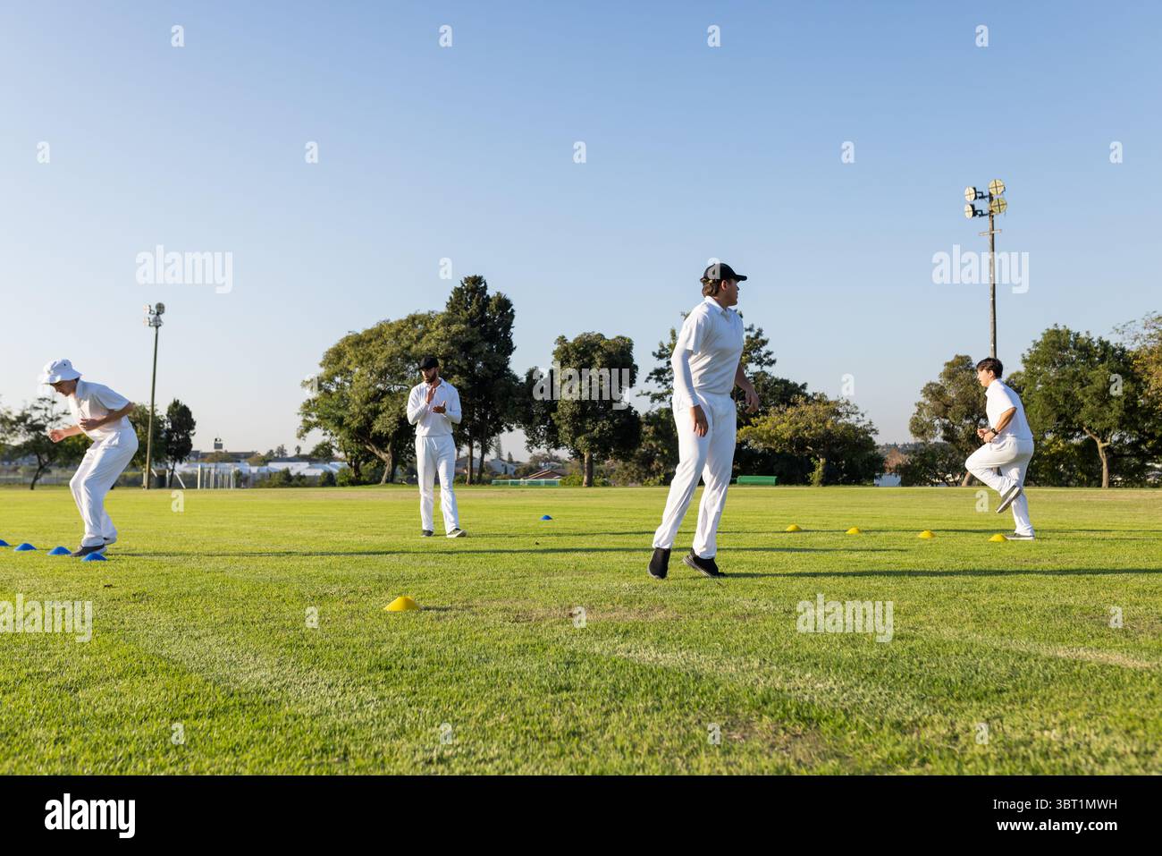 Diverse male players wearing white uniforms fielding on field with ...