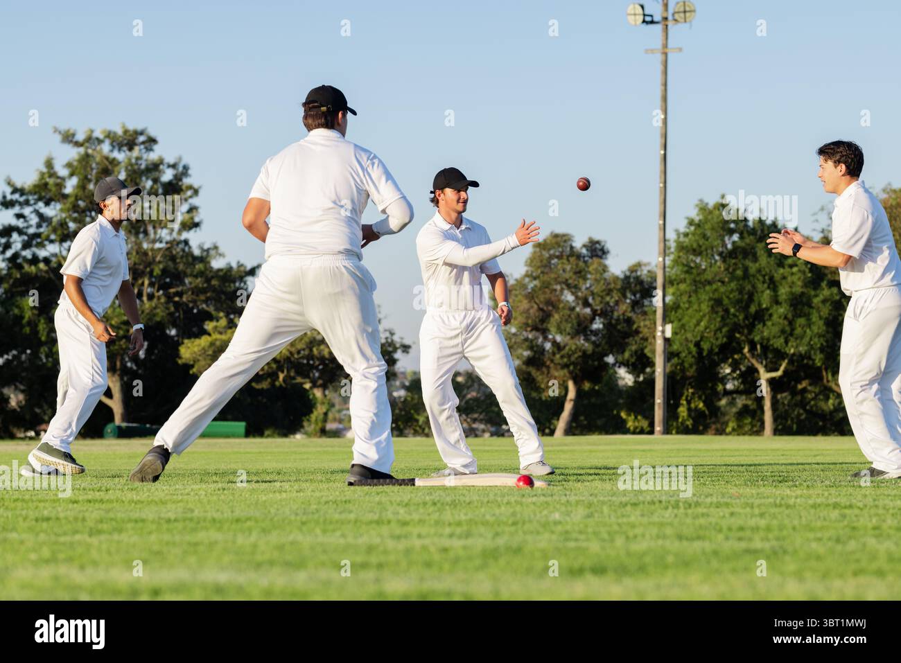 Diverse male teammates standing on grassy field passing red cricket ...