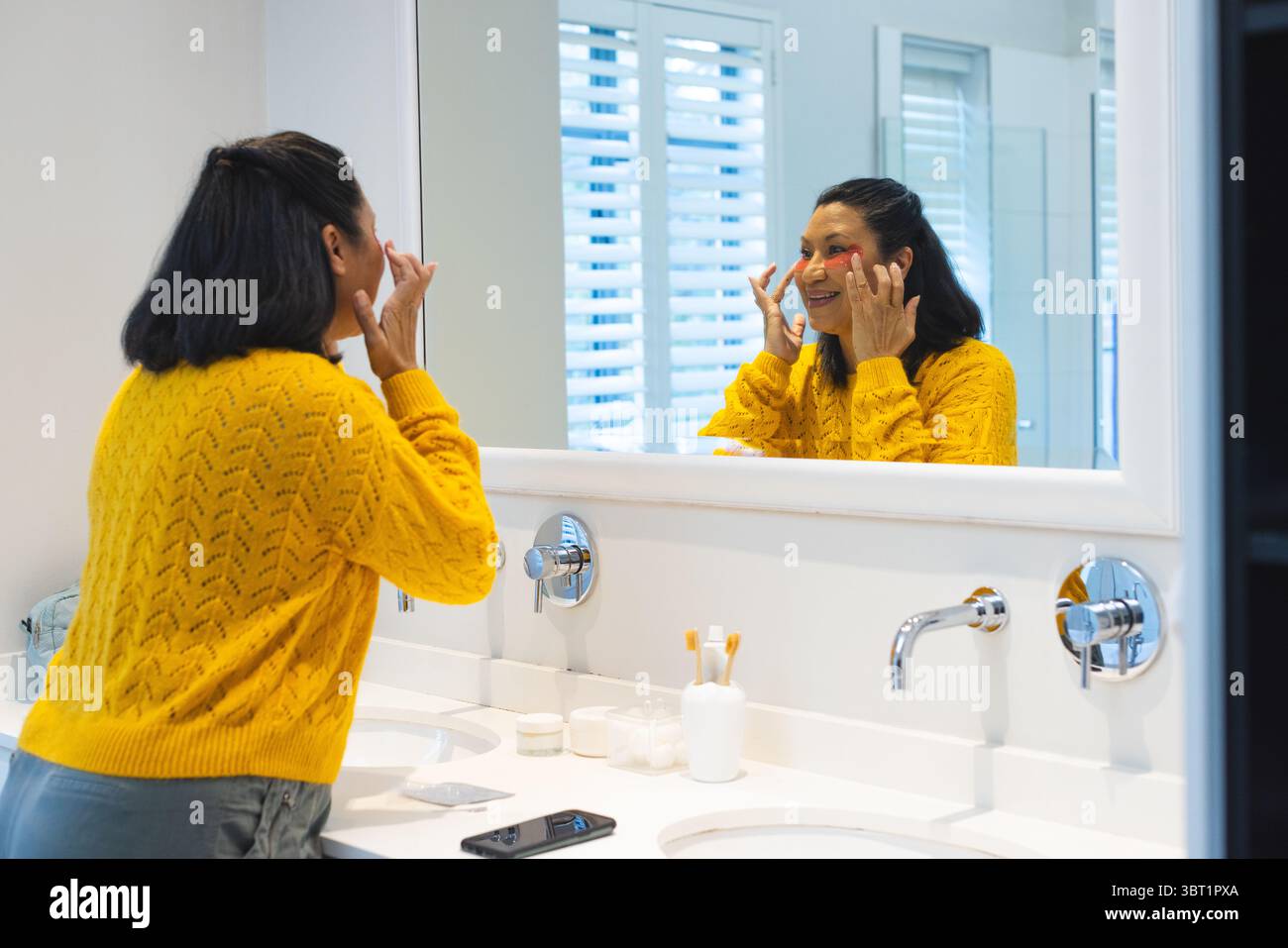 Asian woman wearing yellow sweater placing under-eye patches looking ...