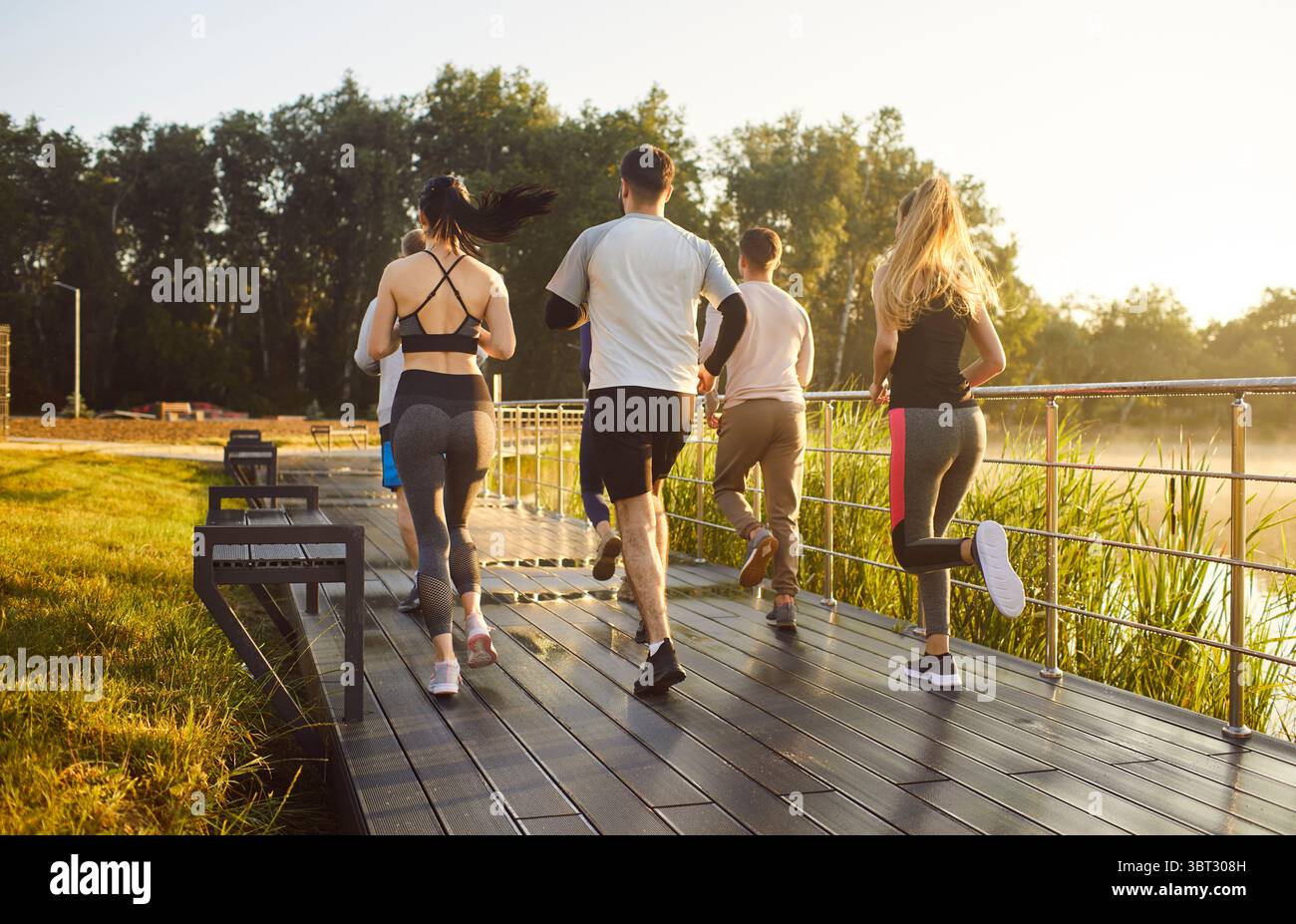 Back view of a team of young people running together in summer park ...