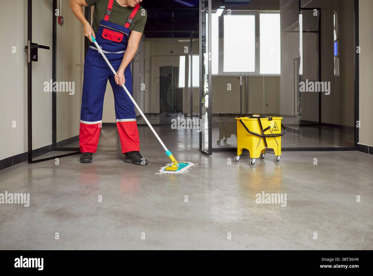 Janitor in uniform mopping floor inside modern commercial building ...