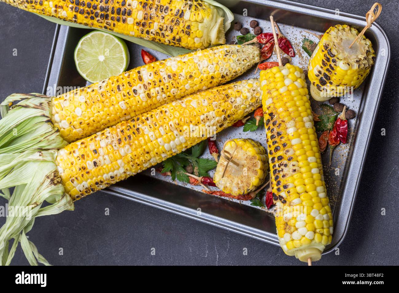 Grilled corn and dried red pepper pods on pallet. Black background. Top ...