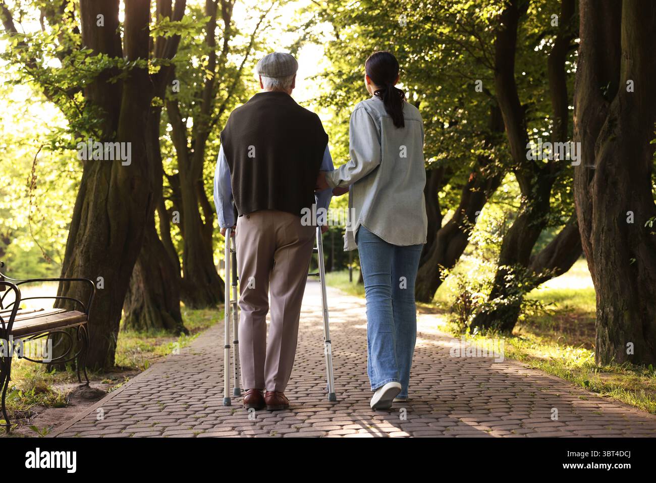 Caregiver supporting elderly man who using walking frame outdoors, back ...