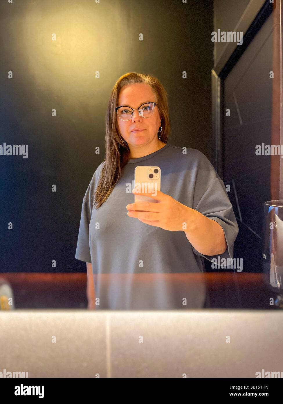Female individual with long brown hair and glasses captures a selfie in ...