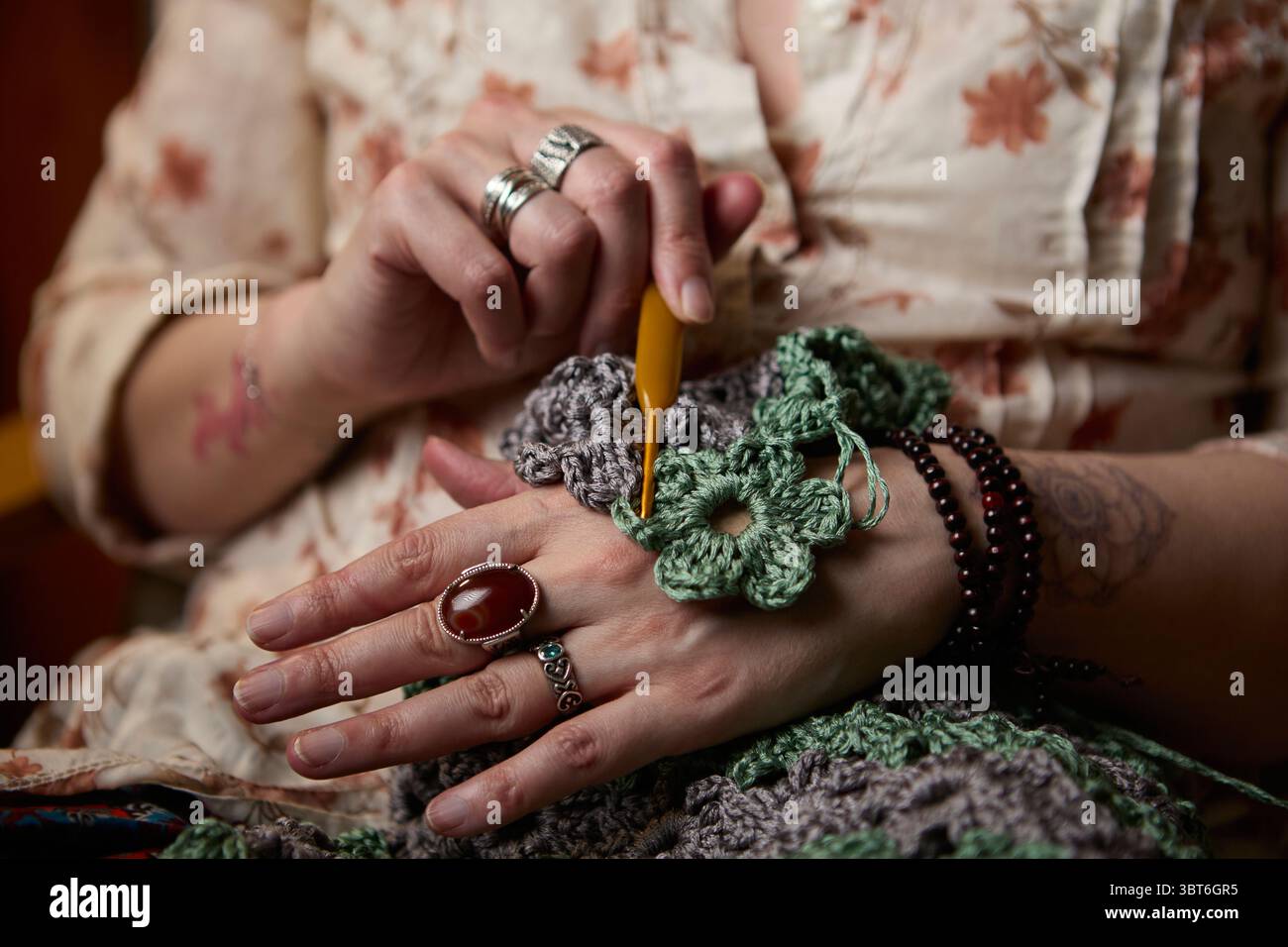 Close-up of a woman crocheting a handmade green and gray floral pattern ...
