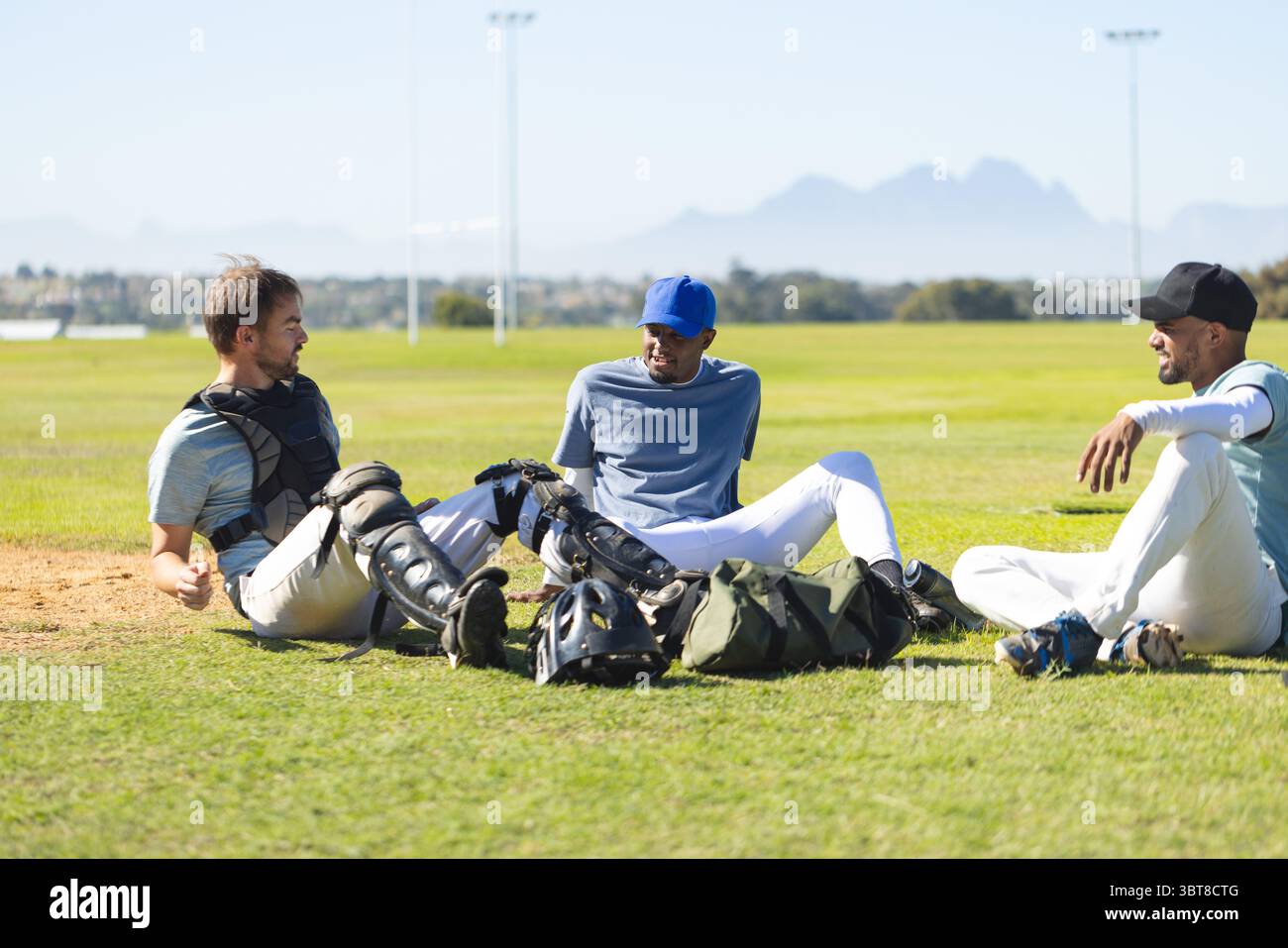 Diverse male teammates sitting and chatting during break on baseball ...