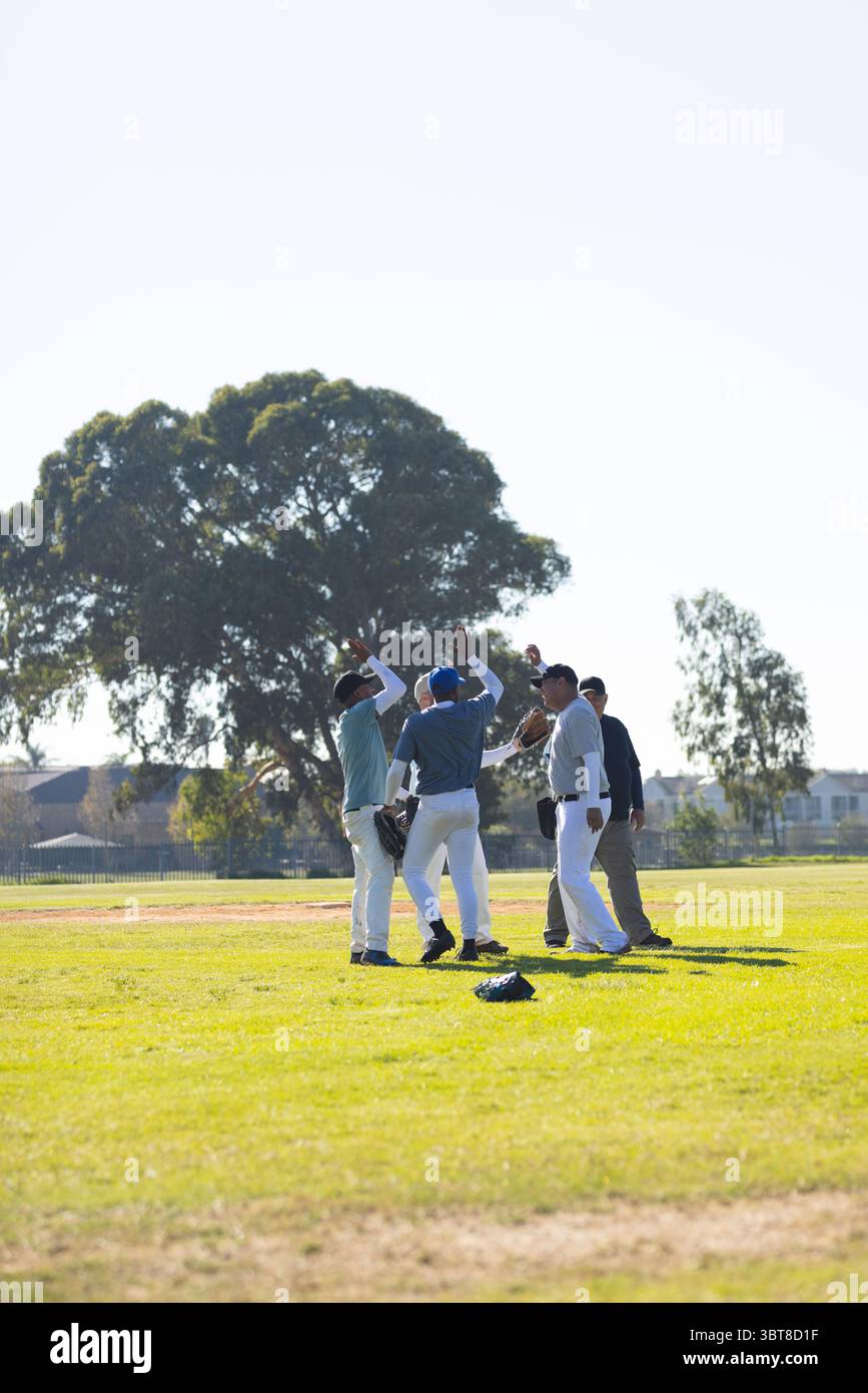 Diverse male baseball teammates exchanging high fives on outfield grass ...