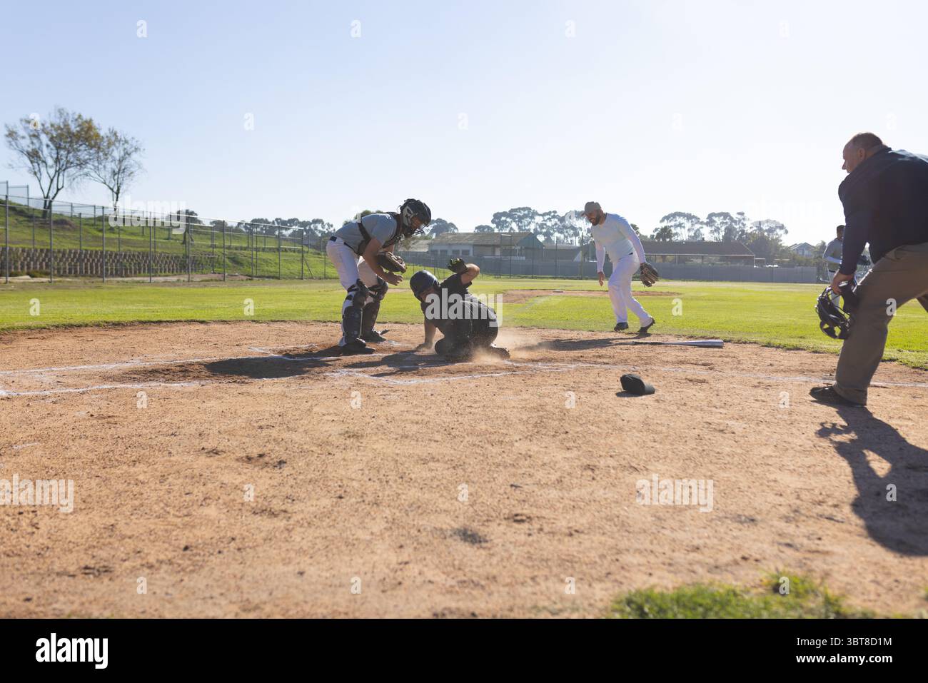 Male baseball players and umpire sliding at home plate while catcher ...
