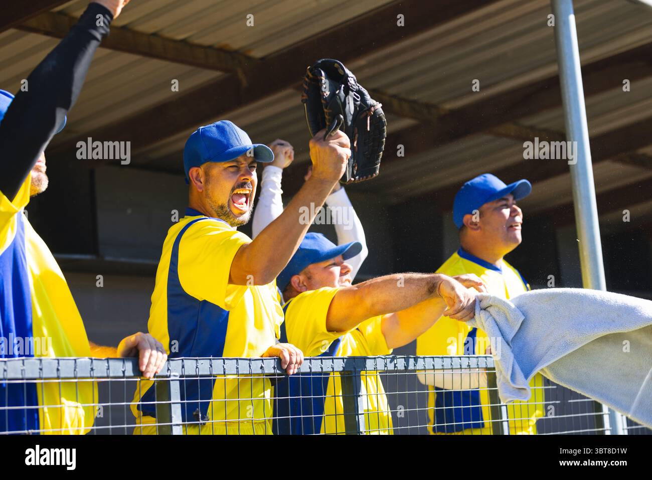 Diverse male baseball teammates raising glove and waving towel while ...