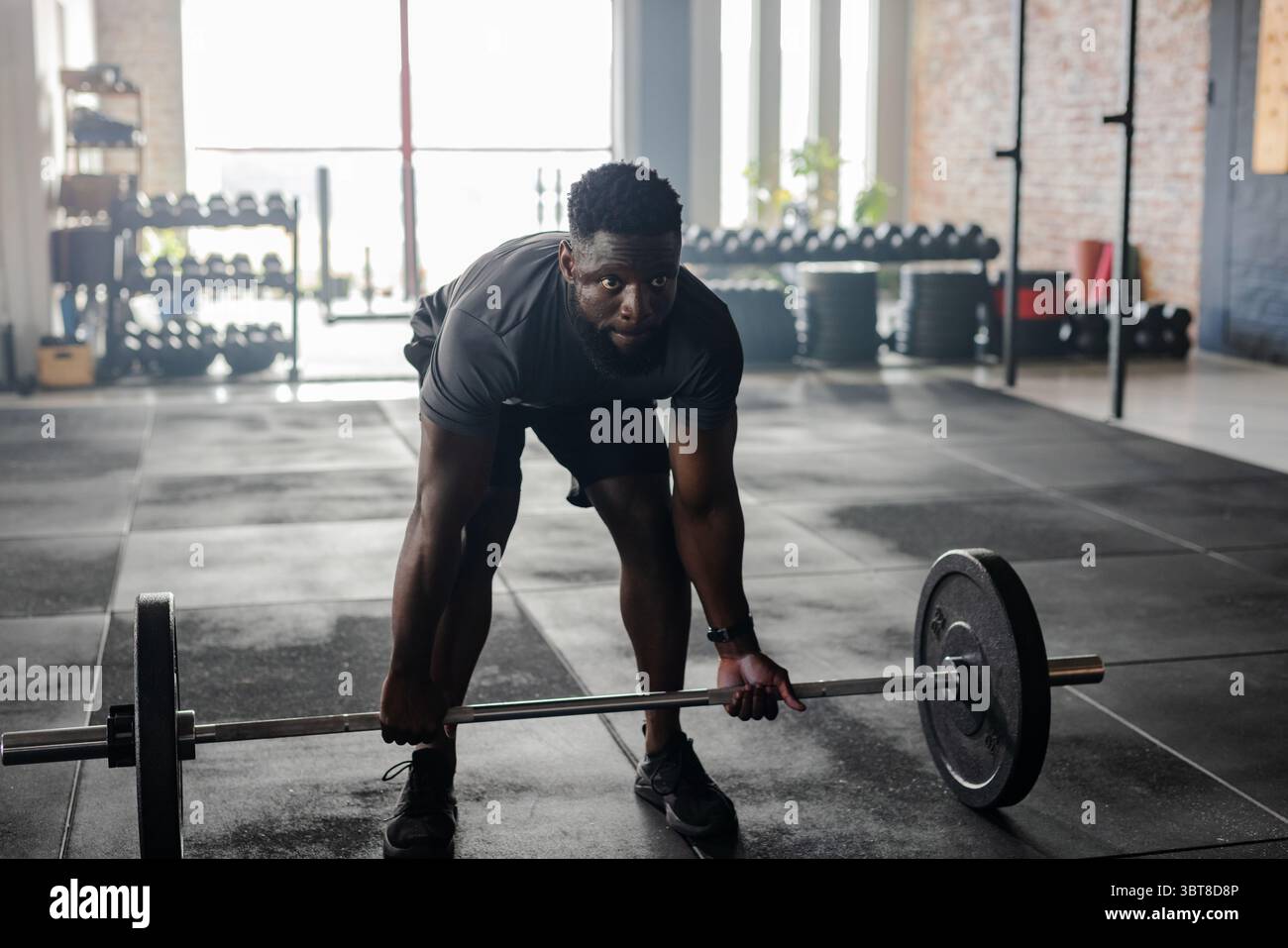 African American male athlete wearing gym clothes lifting loaded ...