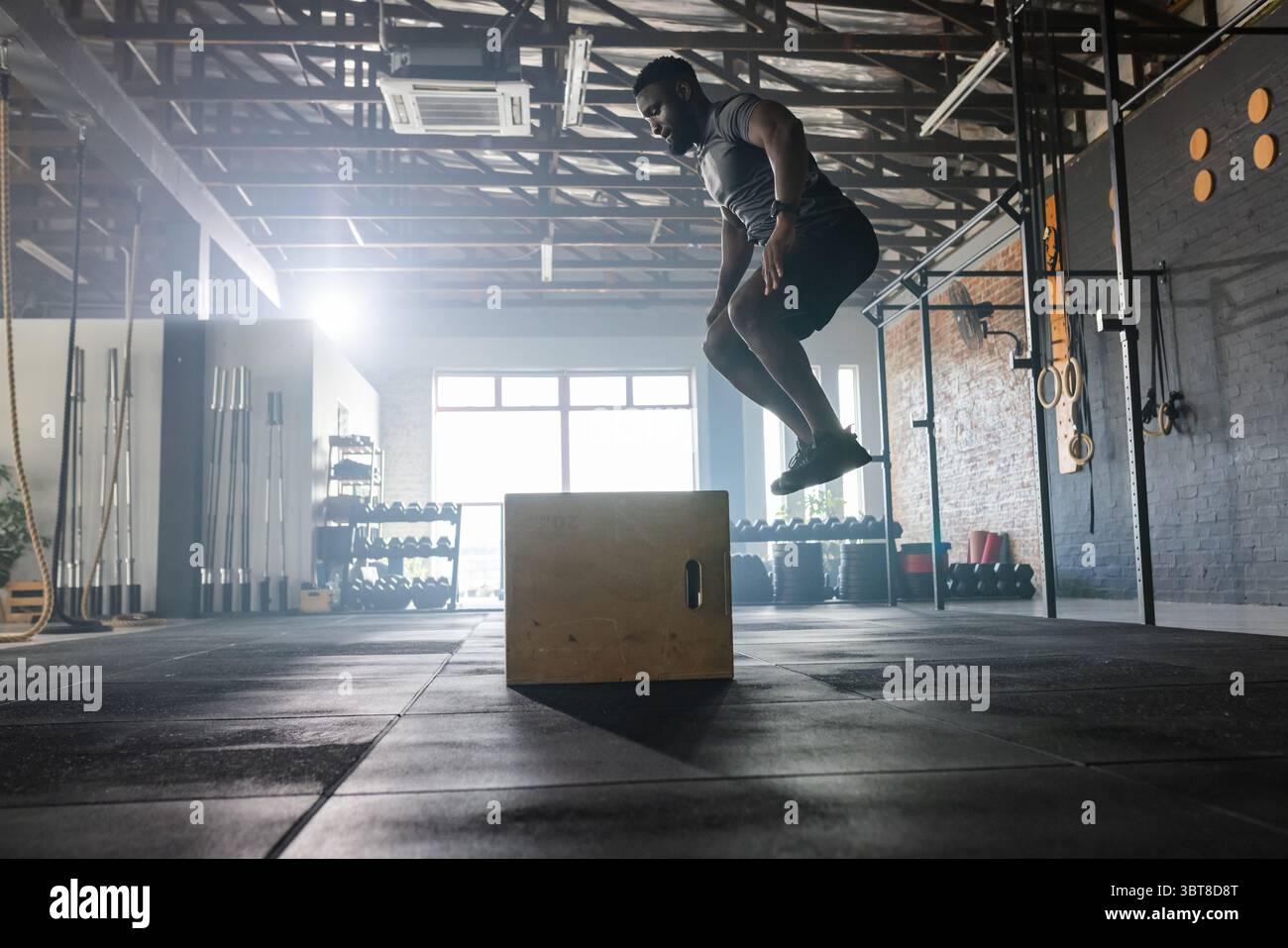 African American man jumping onto wooden plyometric box inside training ...