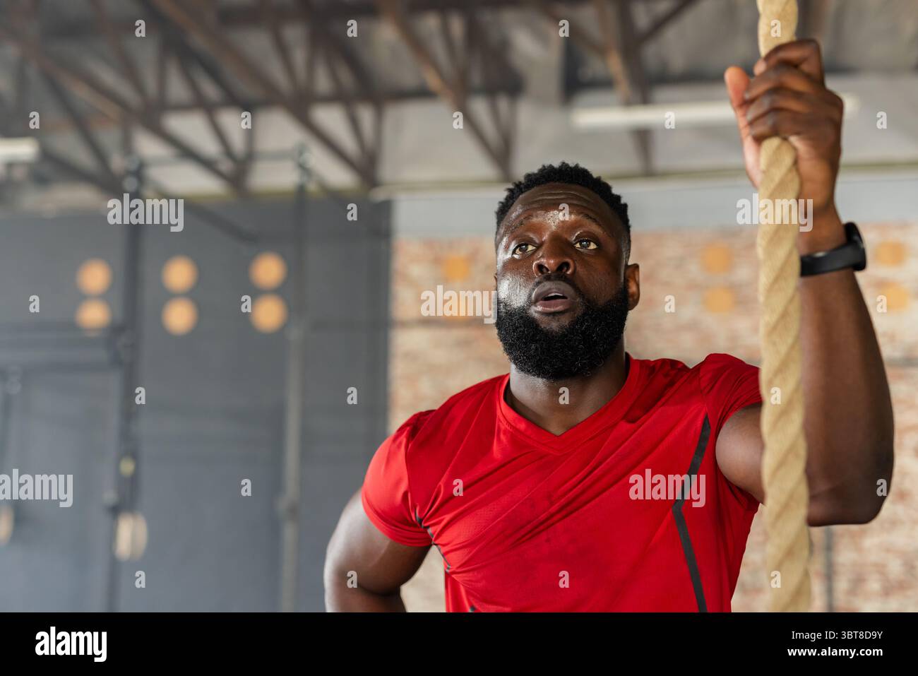 African American man gripping rope and climbing at gym next to ...