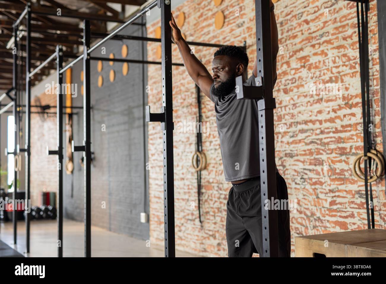 African American man stretching arms overhead, gripping pull-up bar at ...