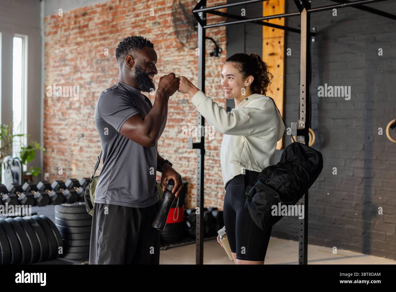 African American trainer and female client fist bumping in gym with ...