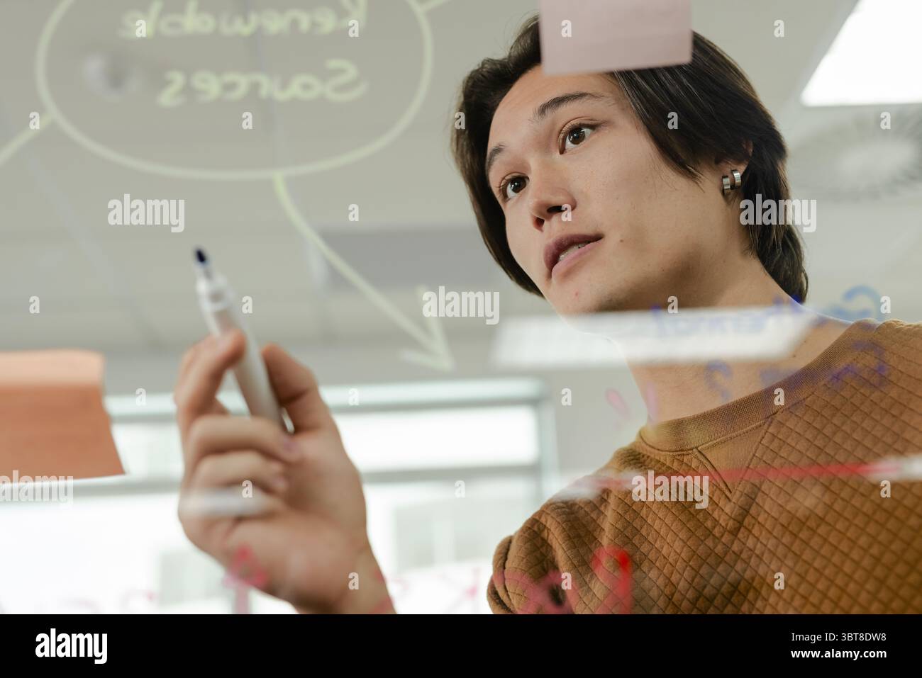 Asian male marking pink sticky notes on glass board with whiteboard ...