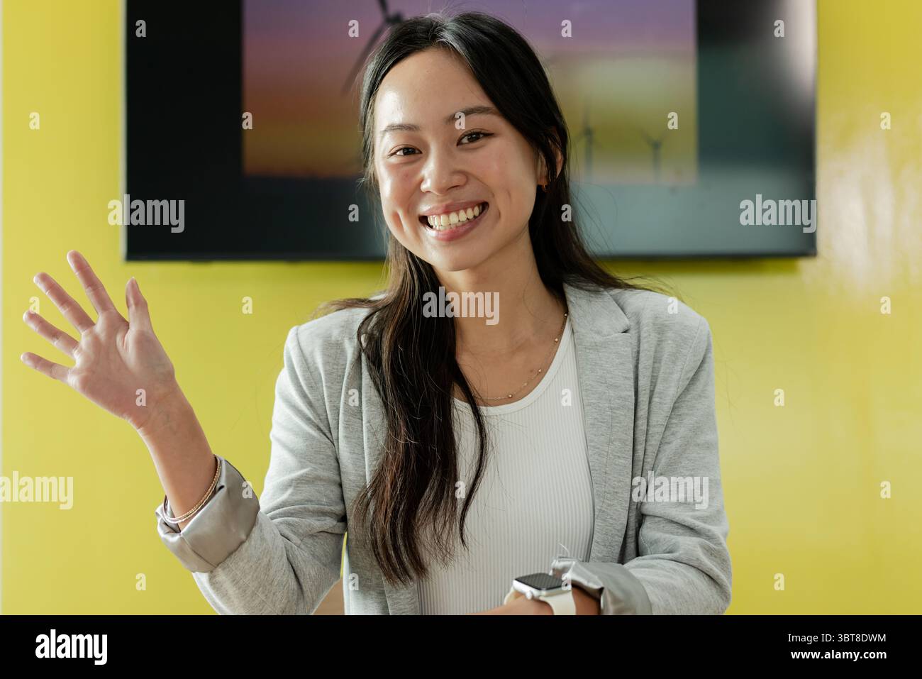 Asian woman smiling and waving in conference room at desk by widescreen ...