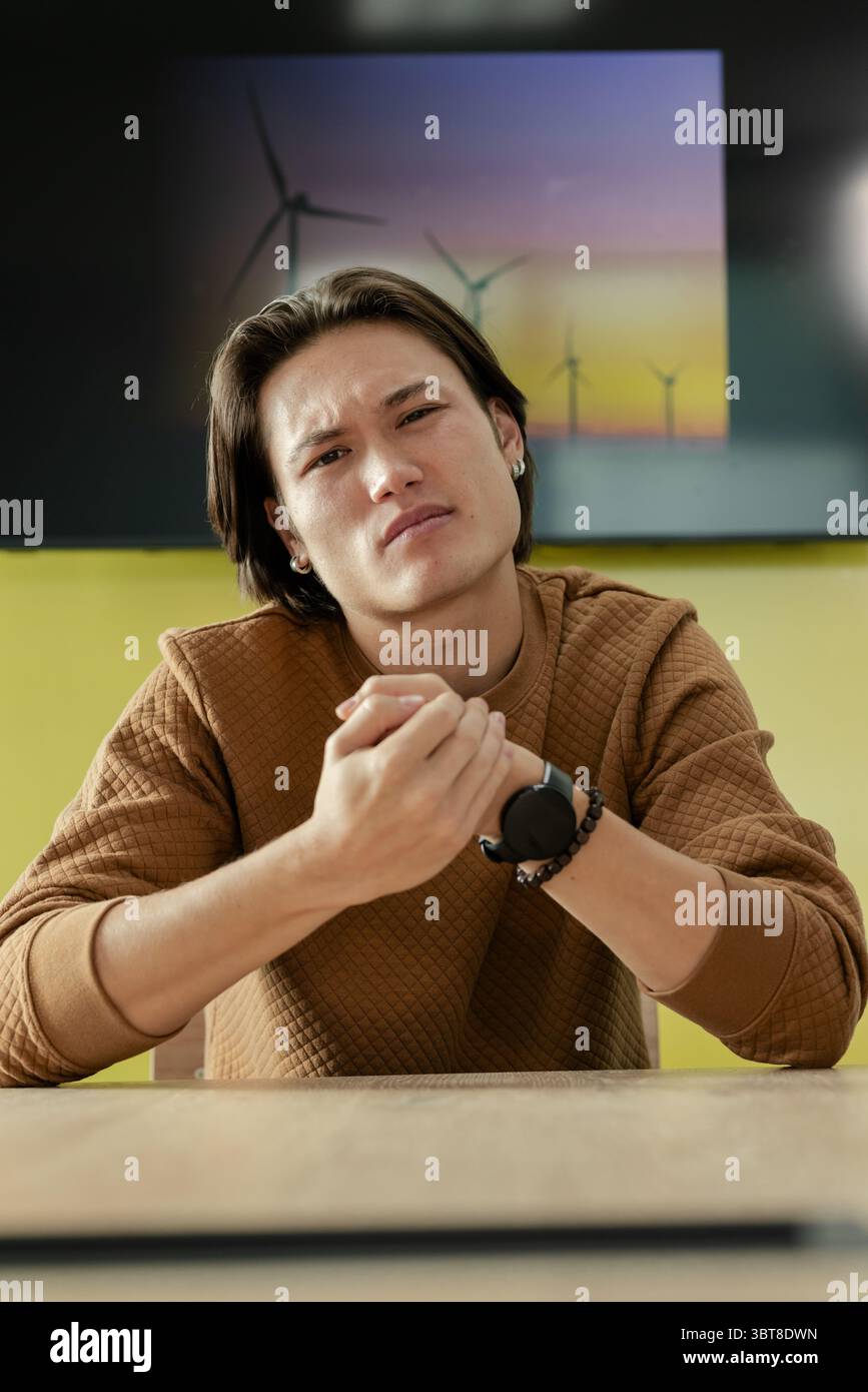 Asian man leaning at conference table wearing smartwatch and bracelet viewing wind turbines ...