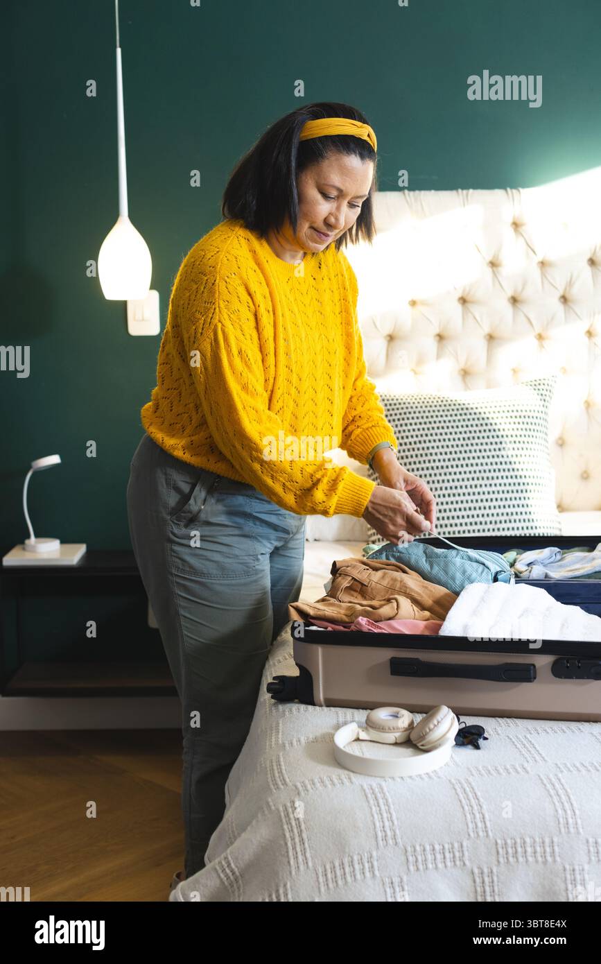 Woman sorting and folding clothes from open suitcase on bed in bedroom ...