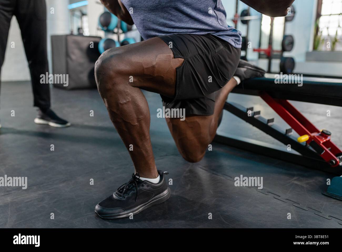 African American client performing split squat on weight bench at gym ...
