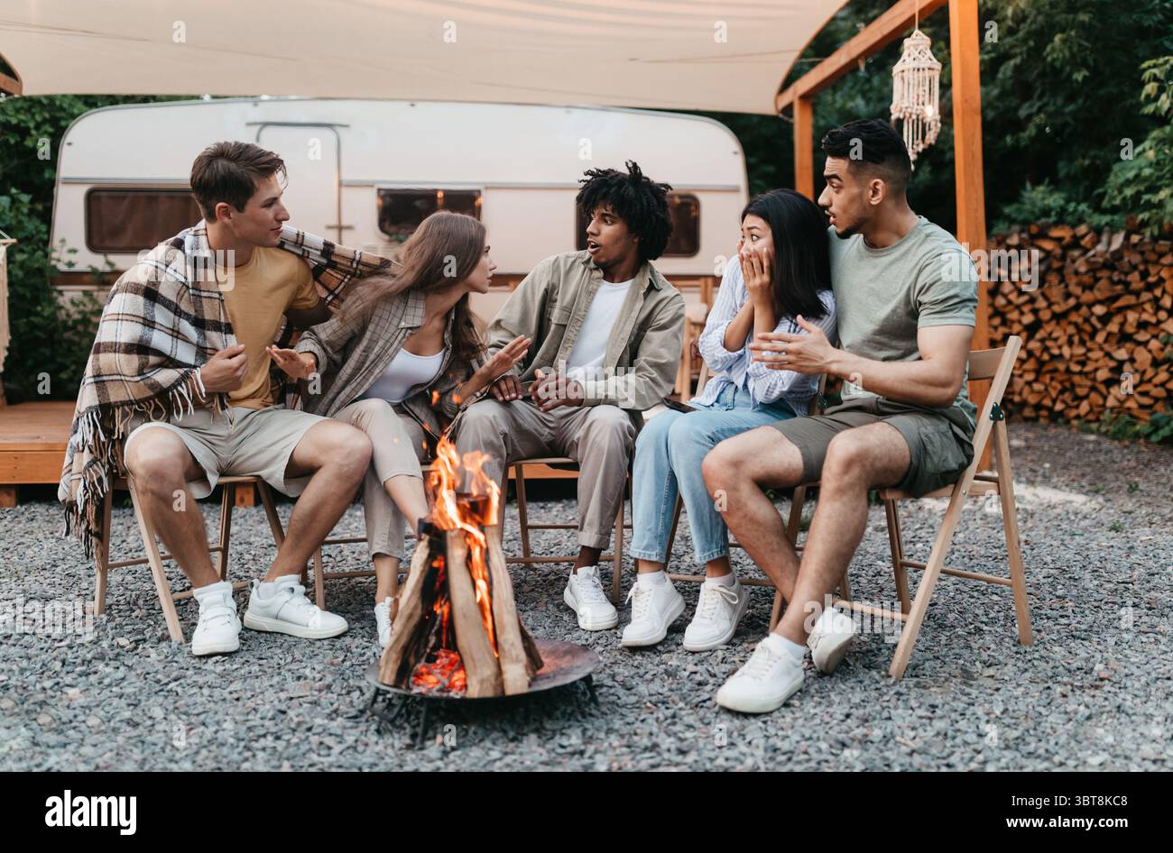 Diverse young friends sitting near campfire, telling scary stories next ...