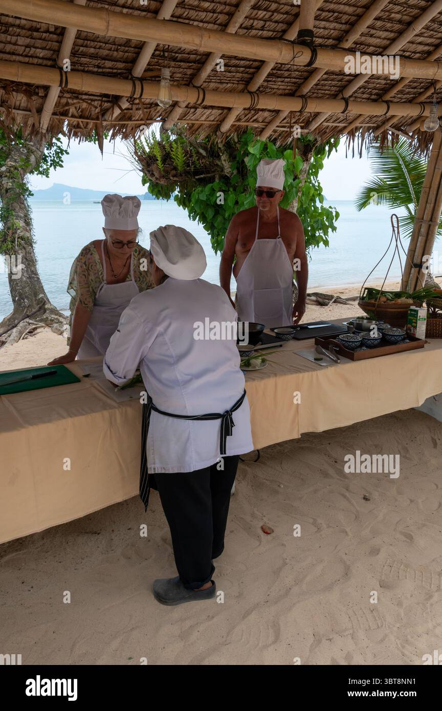 Husband and wife being given a lesson on how to cook a Thai dish by the ...