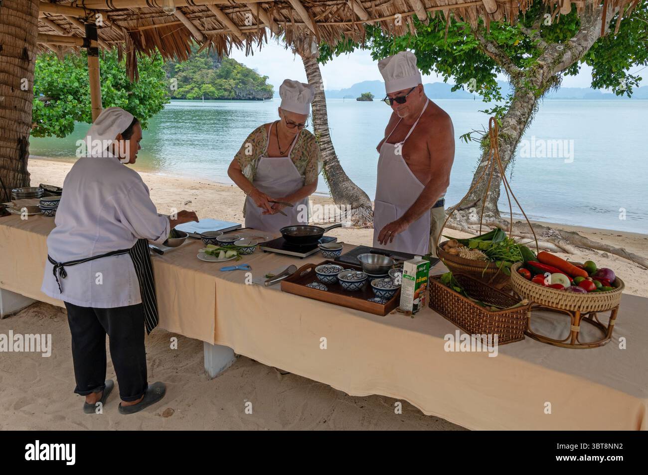 Husband and wife being given a lesson on how to cook a Thai dish by the ...