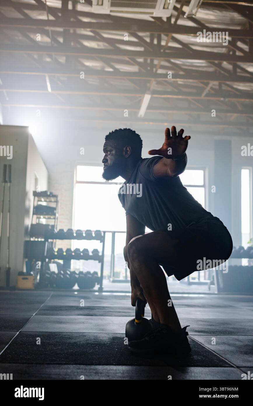 African American man performing kettlebell squat in gym area with ...
