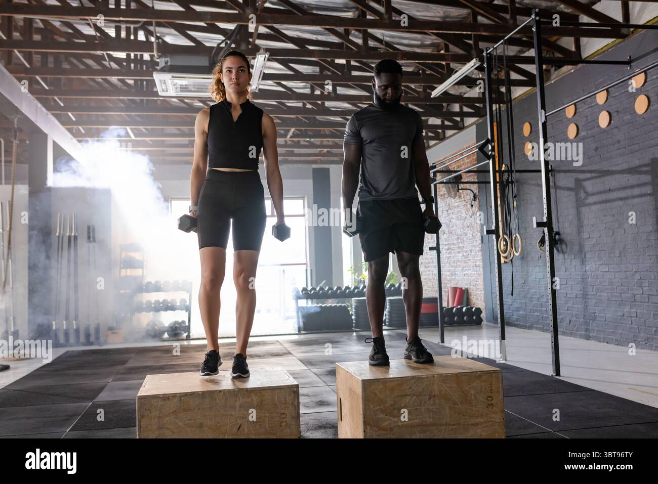 Diverse workout partners standing on plyo boxes in gym holding ...