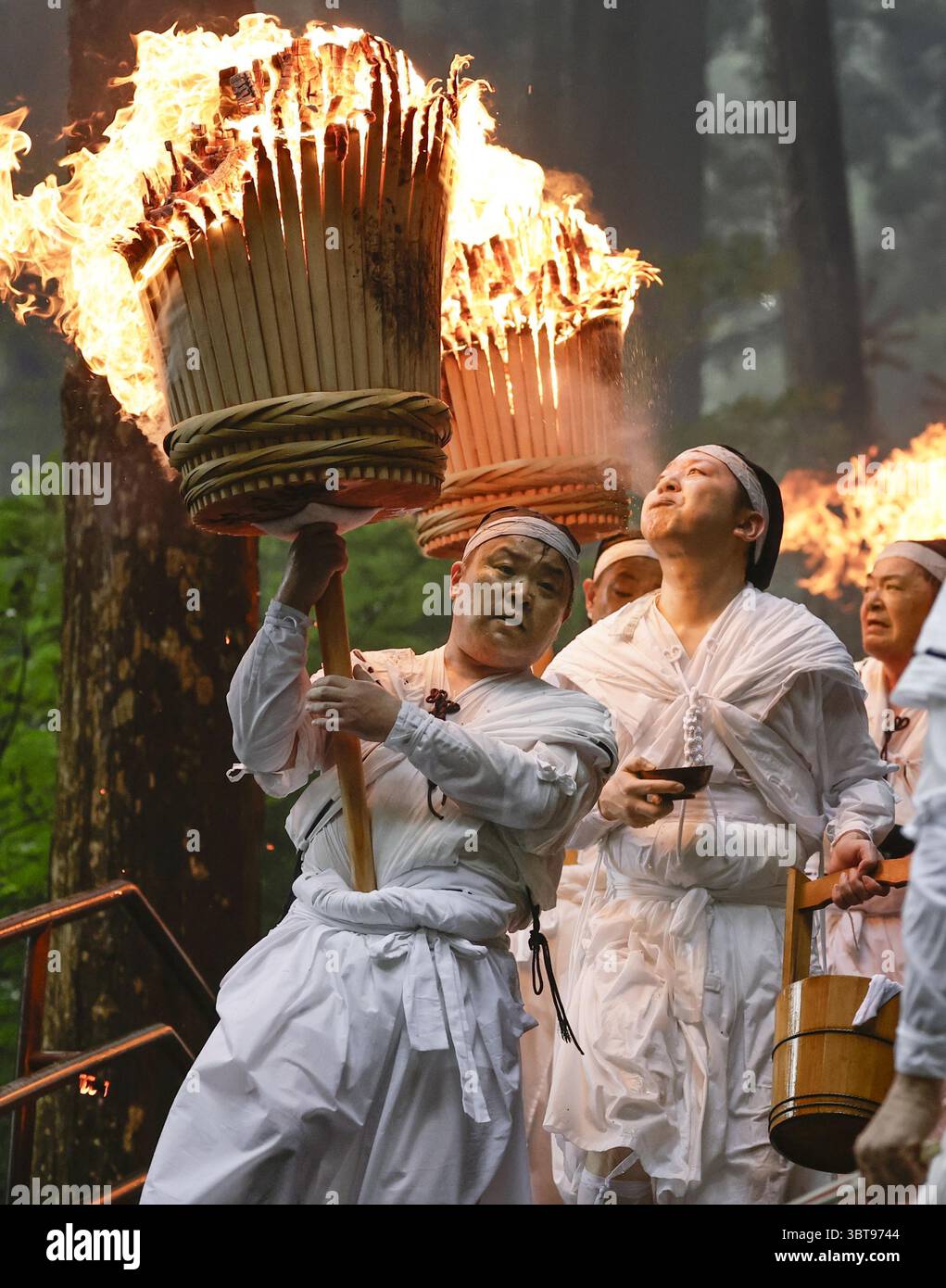 White-robed men hold up flaming torches during an annual fire festival ...