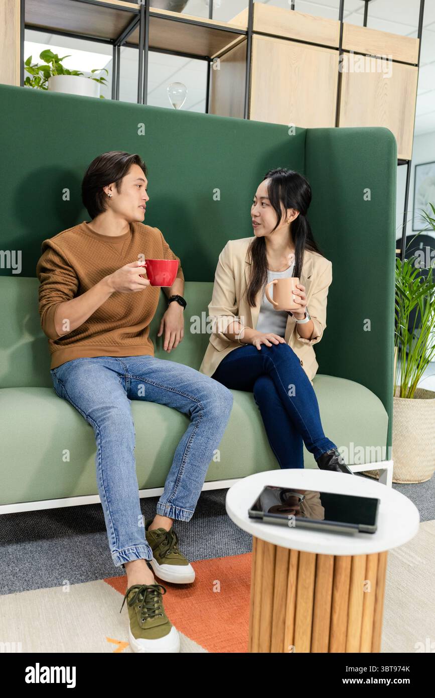 Asian colleagues chatting over coffee while sitting on green booth at ...