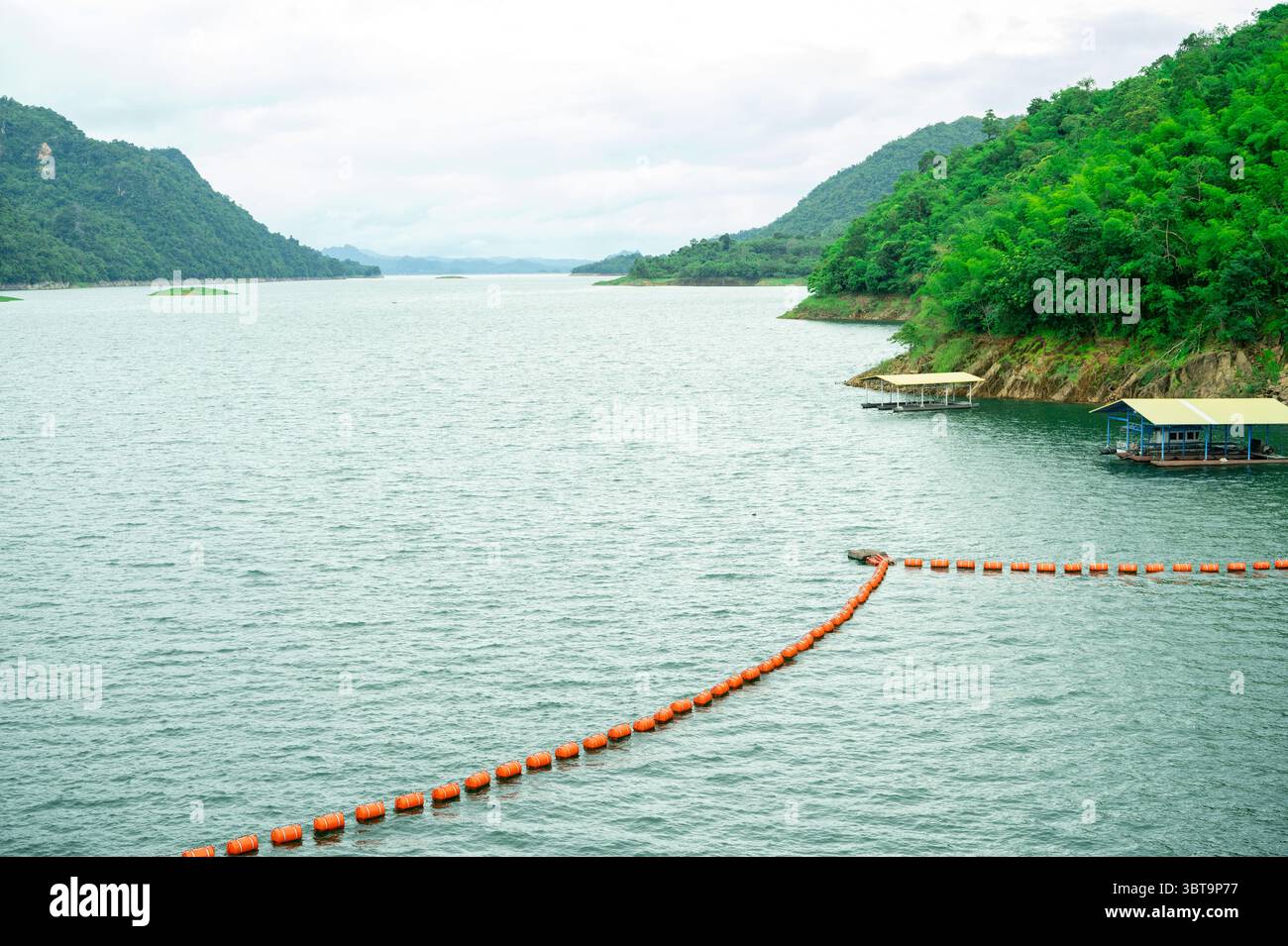 Orange safety buoy line stretching across calm reservoir lake. Green ...