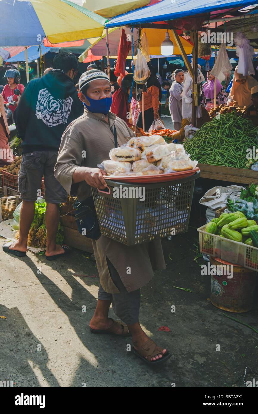 Balikpapan, Indonesia - April 19th 2025. A street vendor carries a ...