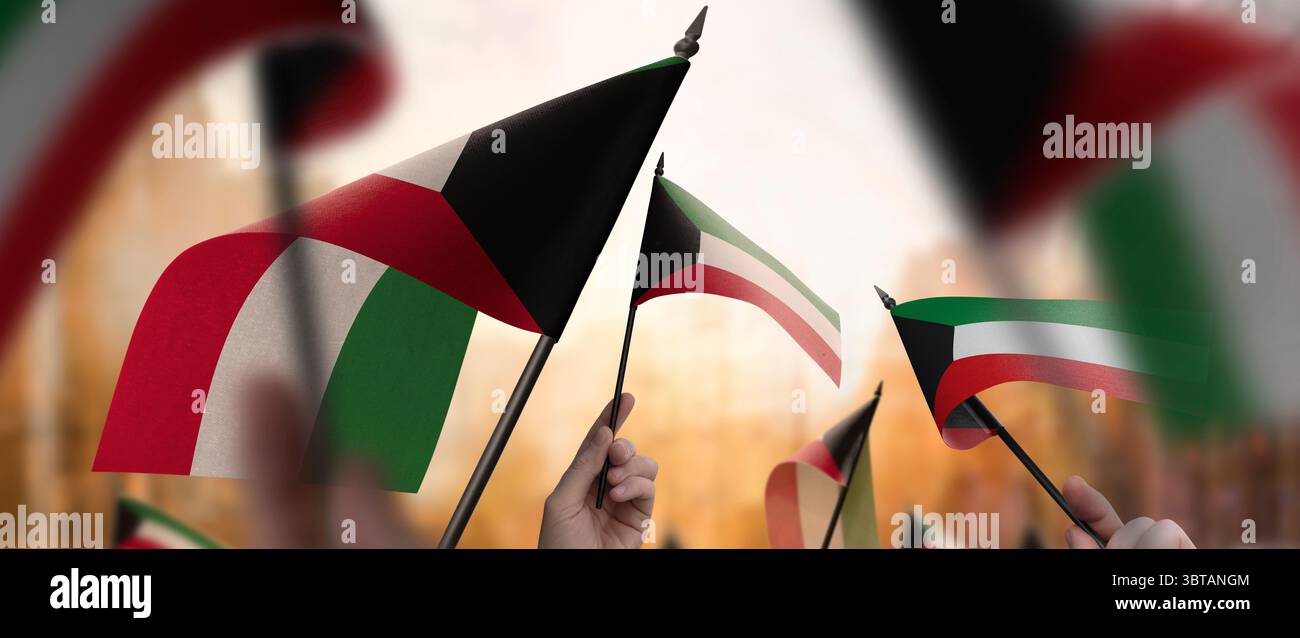 Kuwait flags in their hands on a blurred urban background Stock Photo ...