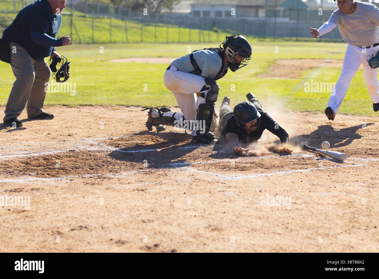 Male baseball players and umpire sliding and tagging at home plate with ...