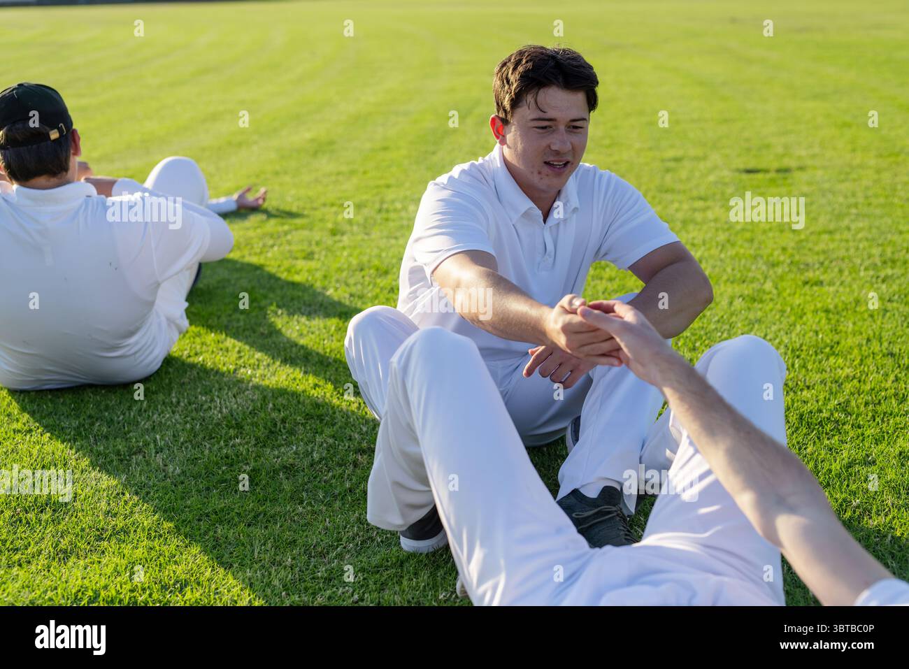 Diverse male teammates performing partner sit-up exercises on grass ...