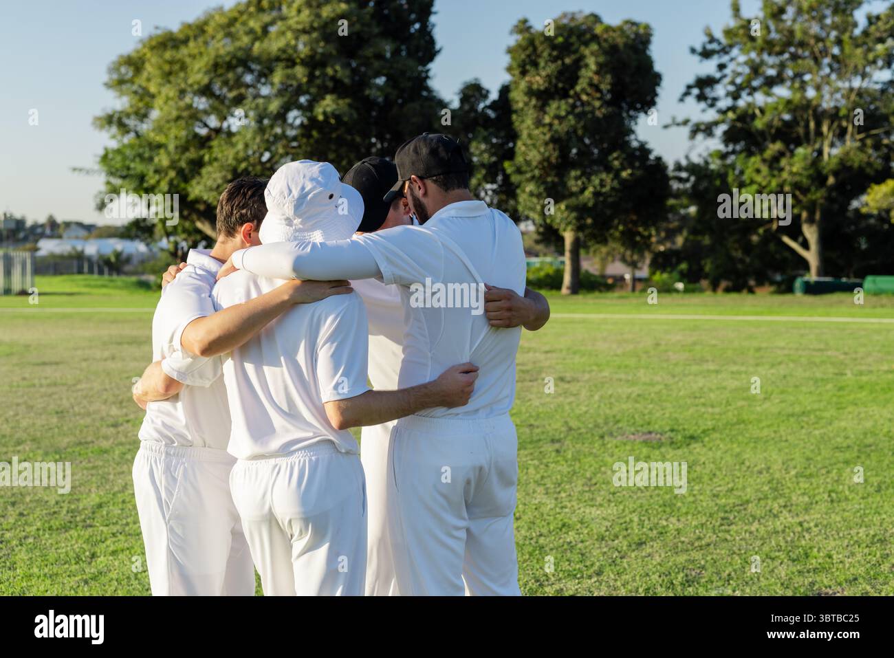 Diverse male teammates huddling on grassy cricket field discussing ...