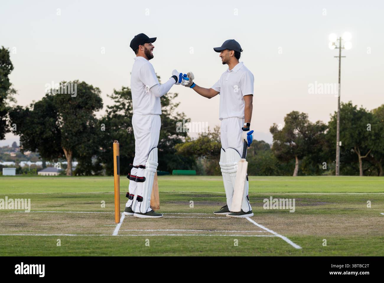 Diverse male cricket teammates standing on grassy pitch holding bats ...