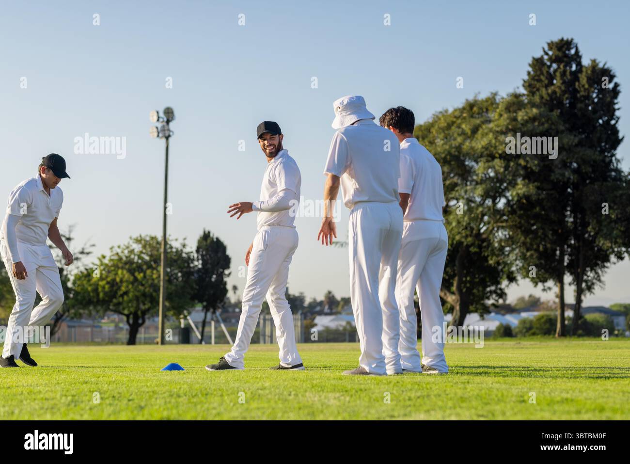 Diverse male cricket teammates practicing drills in white uniforms on ...
