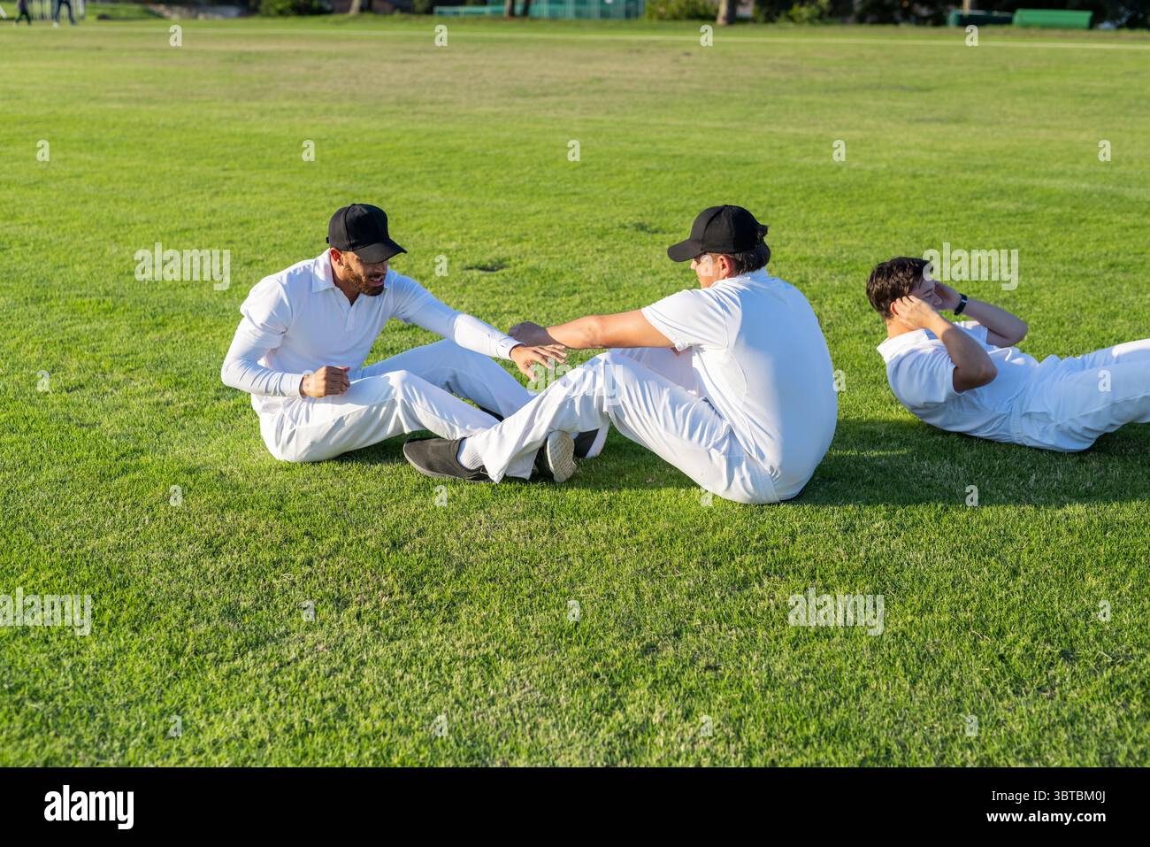 Diverse male teammates performing warm-up on cricket outfield wearing ...