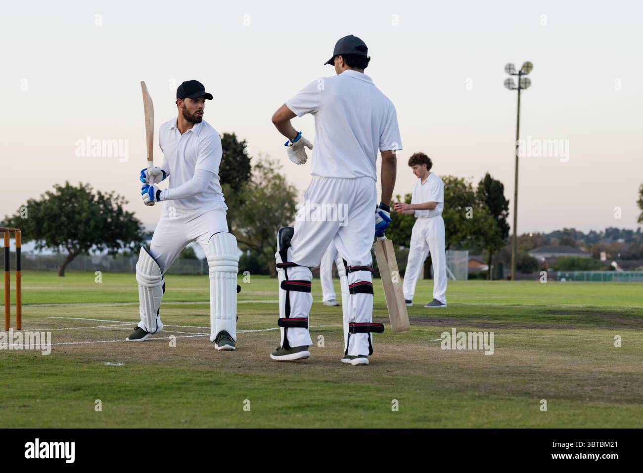 Diverse male teammates playing cricket on suburban sports ground ...