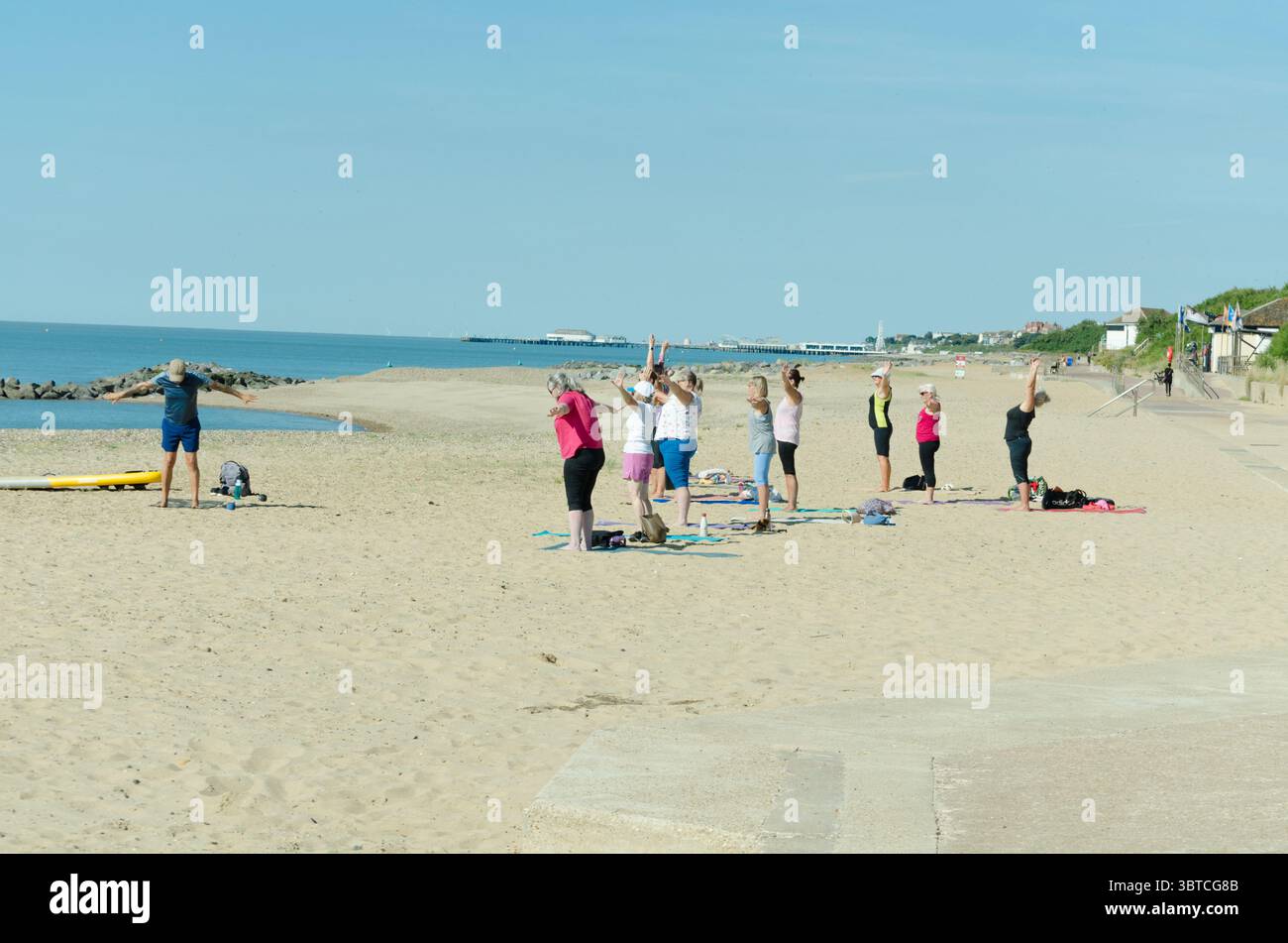 A group of people doing a yoga class and exercising on the beach uk ...