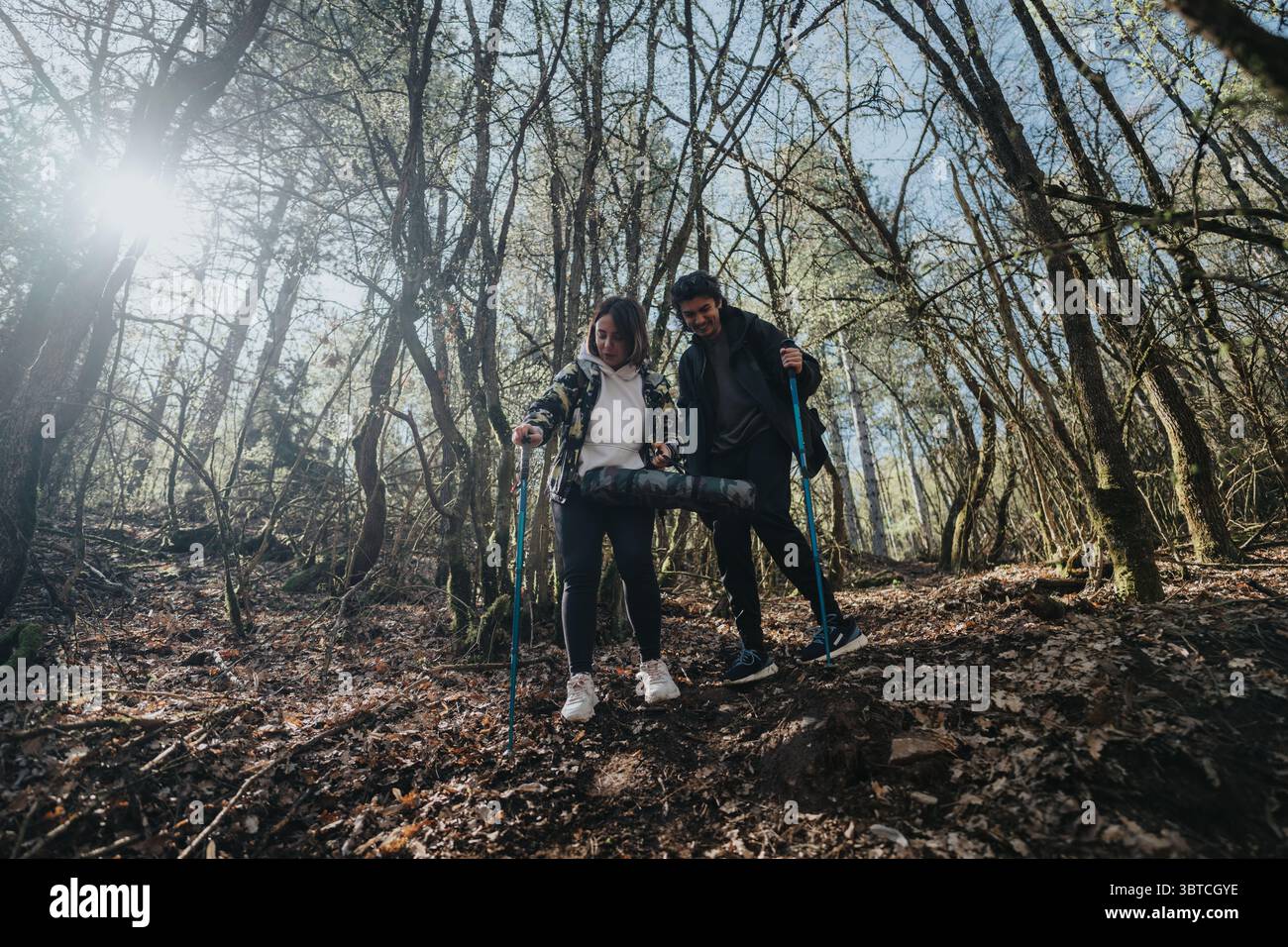 Couple hiking through a sunlit forest using trekking poles on a scenic ...