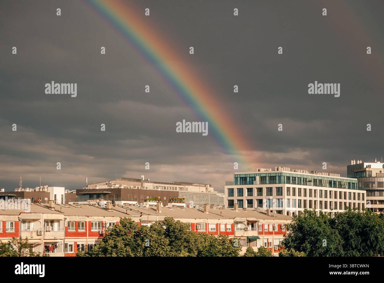 Rainbow arcs over city rooftops beneath stormy skies Stock Photo - Alamy