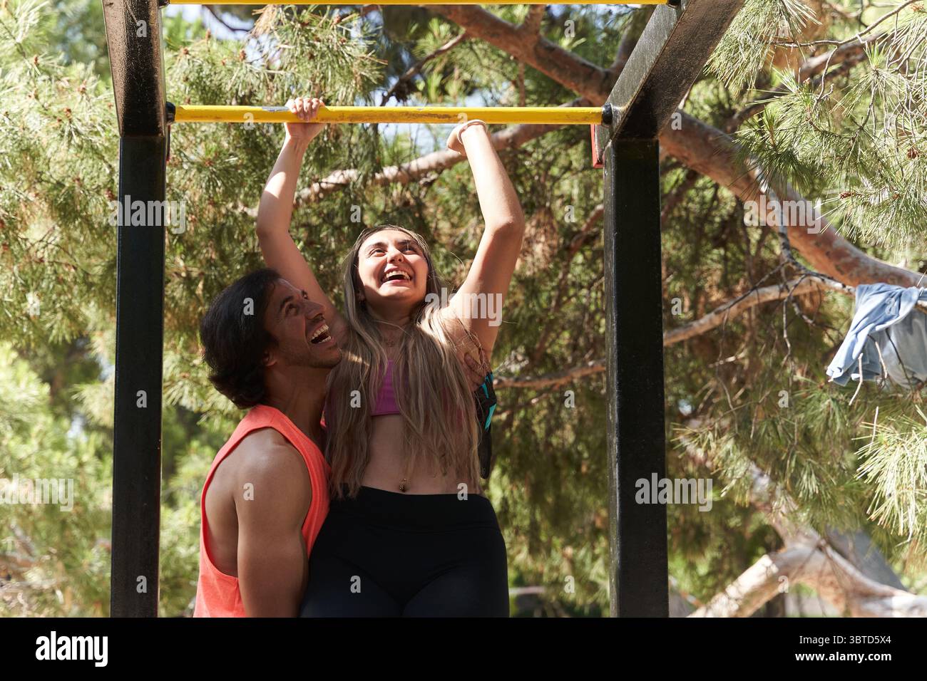 Happy couple laughing while working out on a pull up bar in a park ...