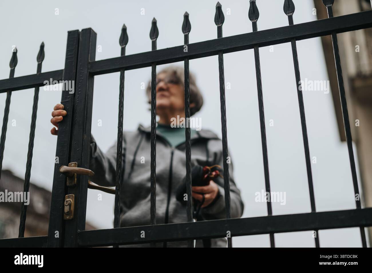 Elderly woman visible through black metal gate in an urban outdoor ...