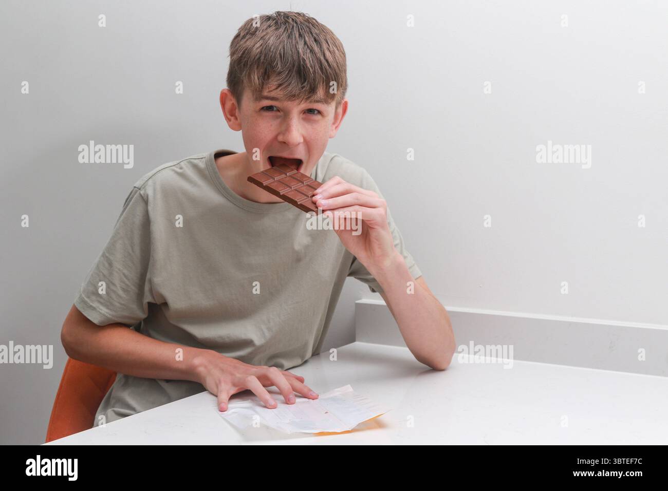Teenage boy eating a bar of chocolate at a kitchen counter Stock Photo ...
