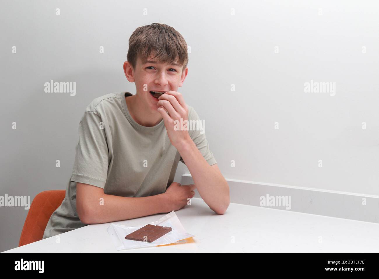 Teenage boy eating a bar of chocolate at a kitchen counter Stock Photo ...